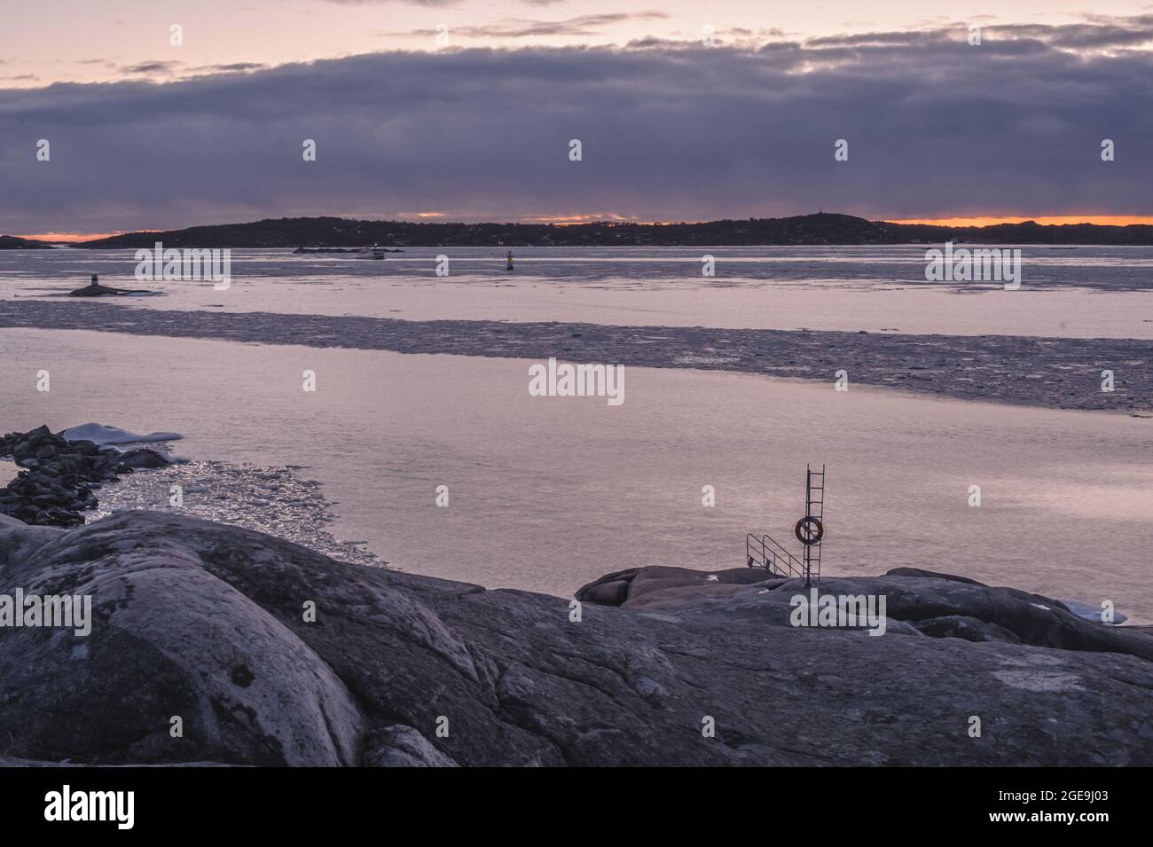 cliffs by an icy fjord at winter. Ferry in the background, after sunset ...