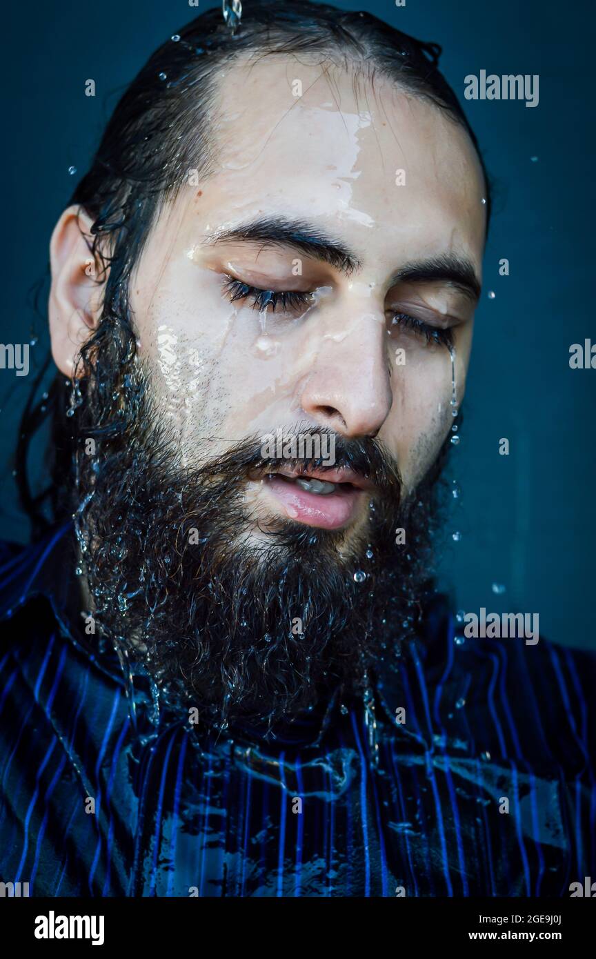Portrait of a young bearded man who refreshes himself by pouring water ...