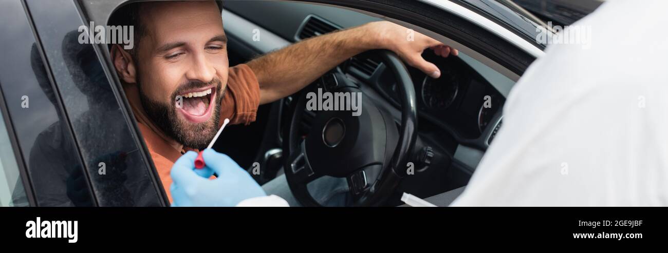 Medical worker holding pcr test near driver with open mouth in car ...