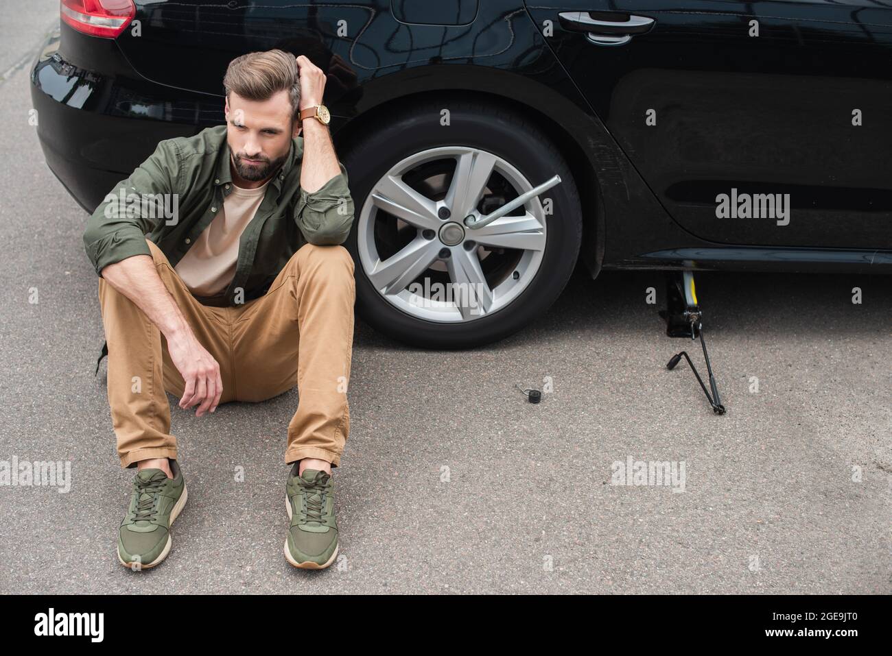 Sad driver sitting near lift jack and wrench in wheel of auto Stock ...
