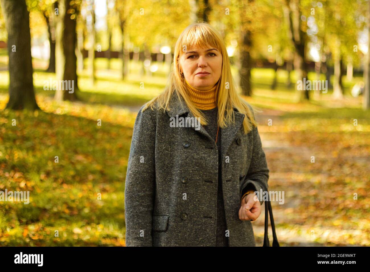 Defocus serious blond 40s woman posing in yellow autumn park. Happy ...