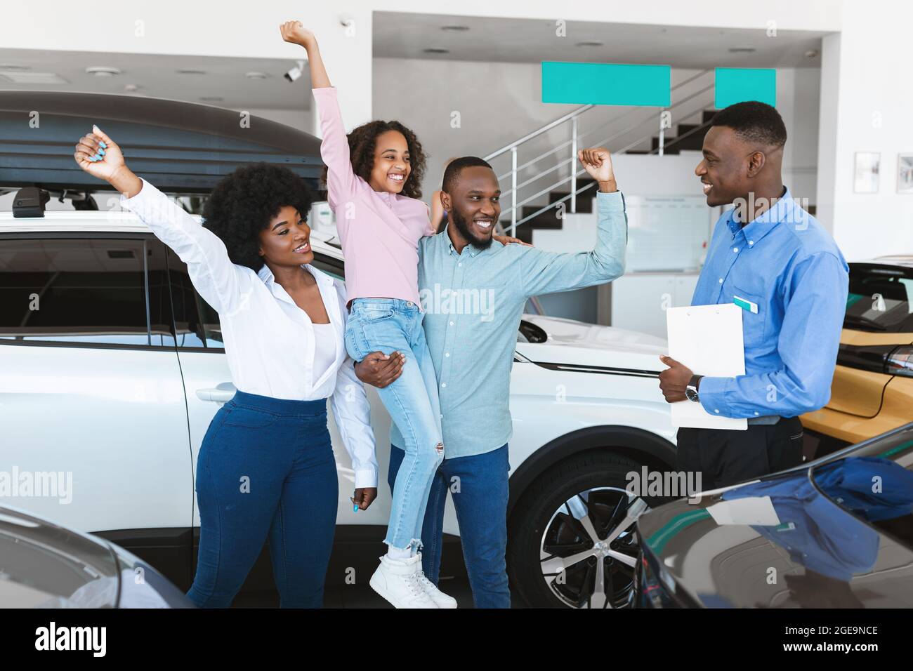 Black family feeling excited over buying auto, raising hands, gesturing YES, standing with car ...