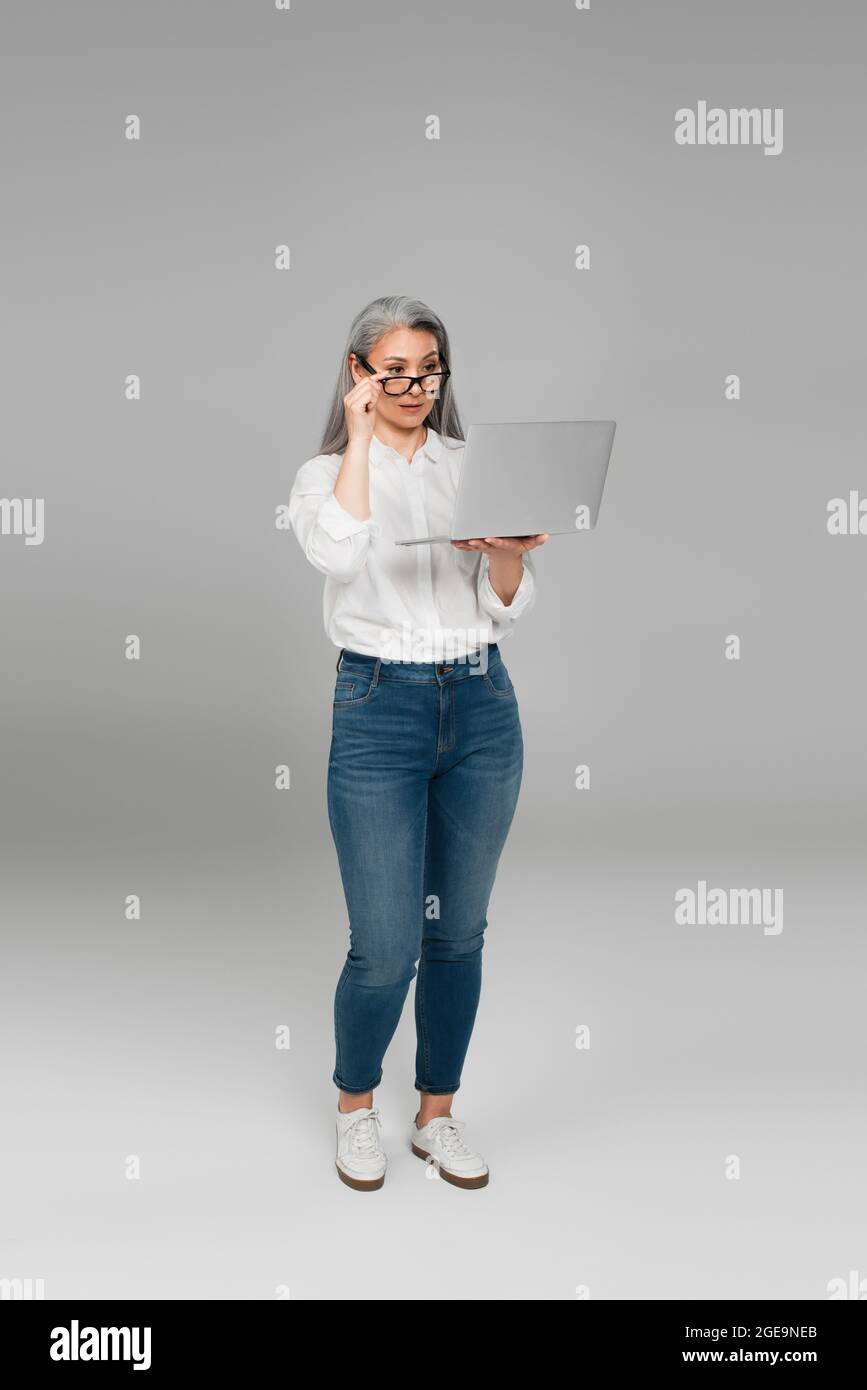 full length view of middle aged woman adjusting eyeglasses while ...