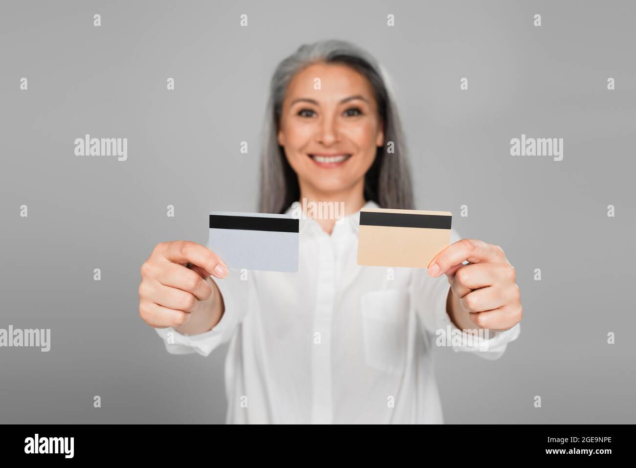 blurred mature woman smiling while showing credit cards isolated on ...