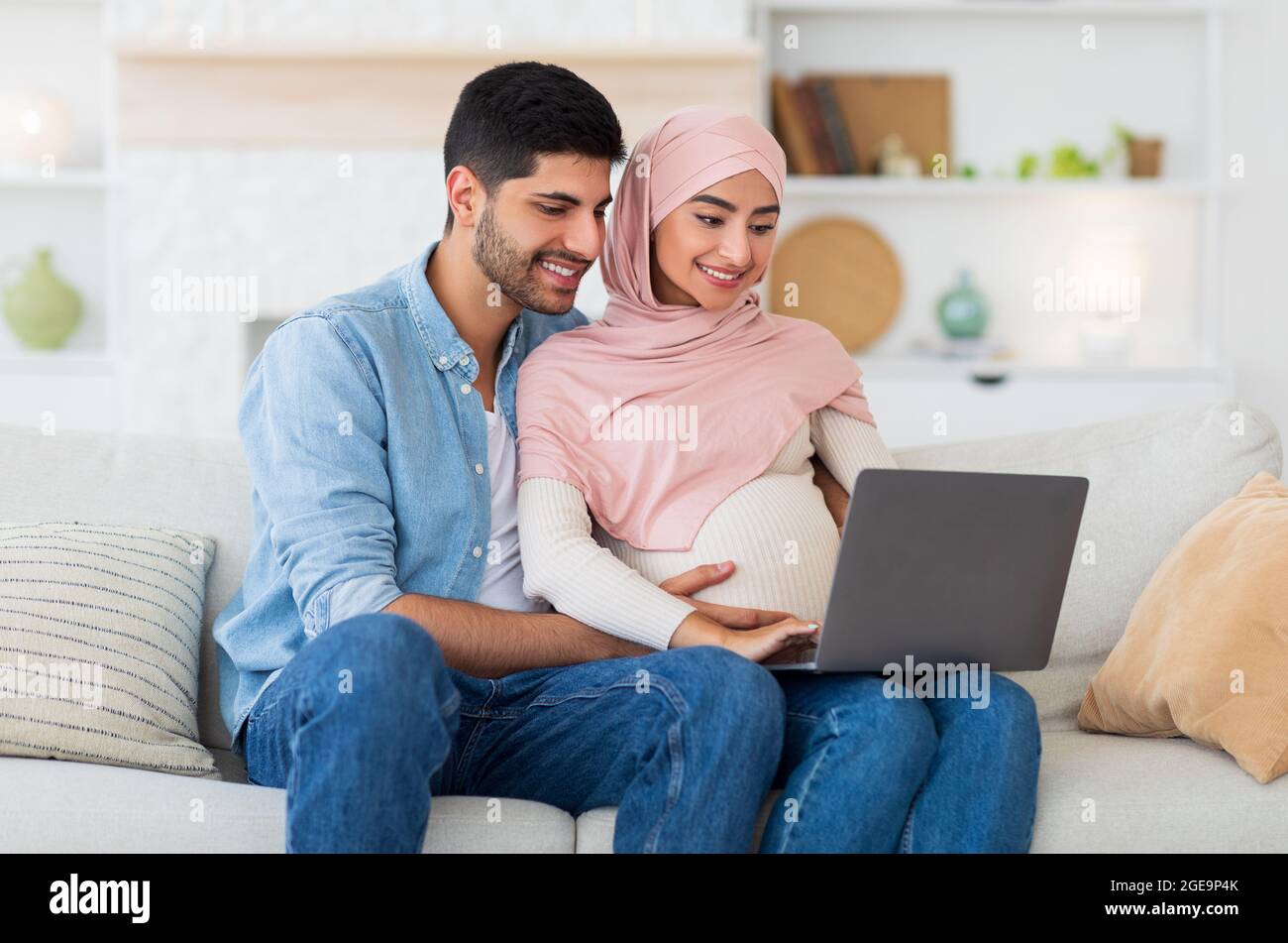 Loving pregnant muslim couple using laptop computer, resting on sofa in ...