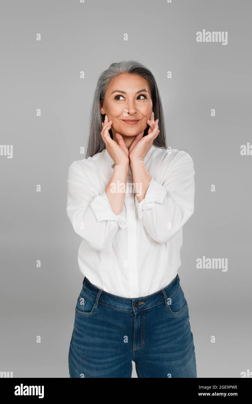 sly woman in white shirt touching face while looking aside isolated on ...