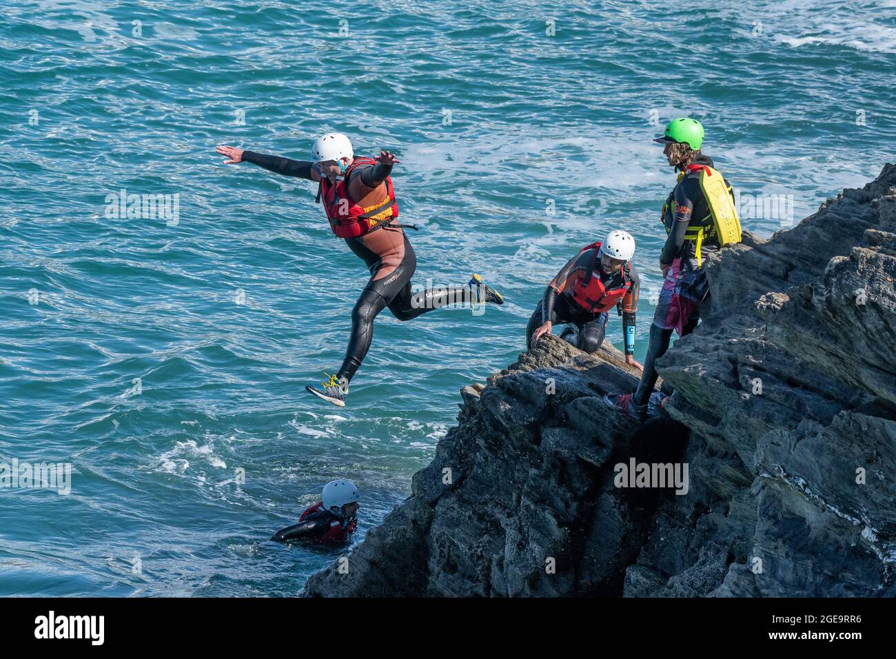 Holidaymakers jumping off rocks coasteering with a guide on Towan Head ...