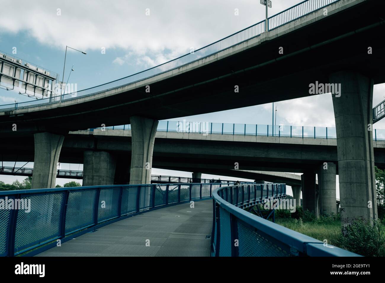 Pedestrian bridge with blue fences under two concrete bridges with ...