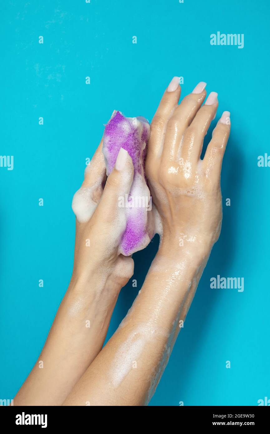 Hand of crop anonymous female squeezing bath sponge with white foam ...