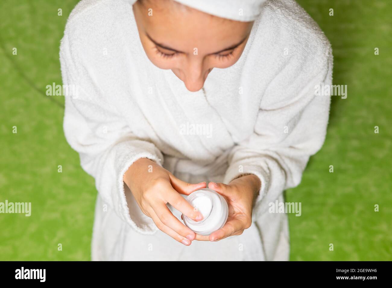 Top view of young female in white bathrobe sitting on bed and taking ...