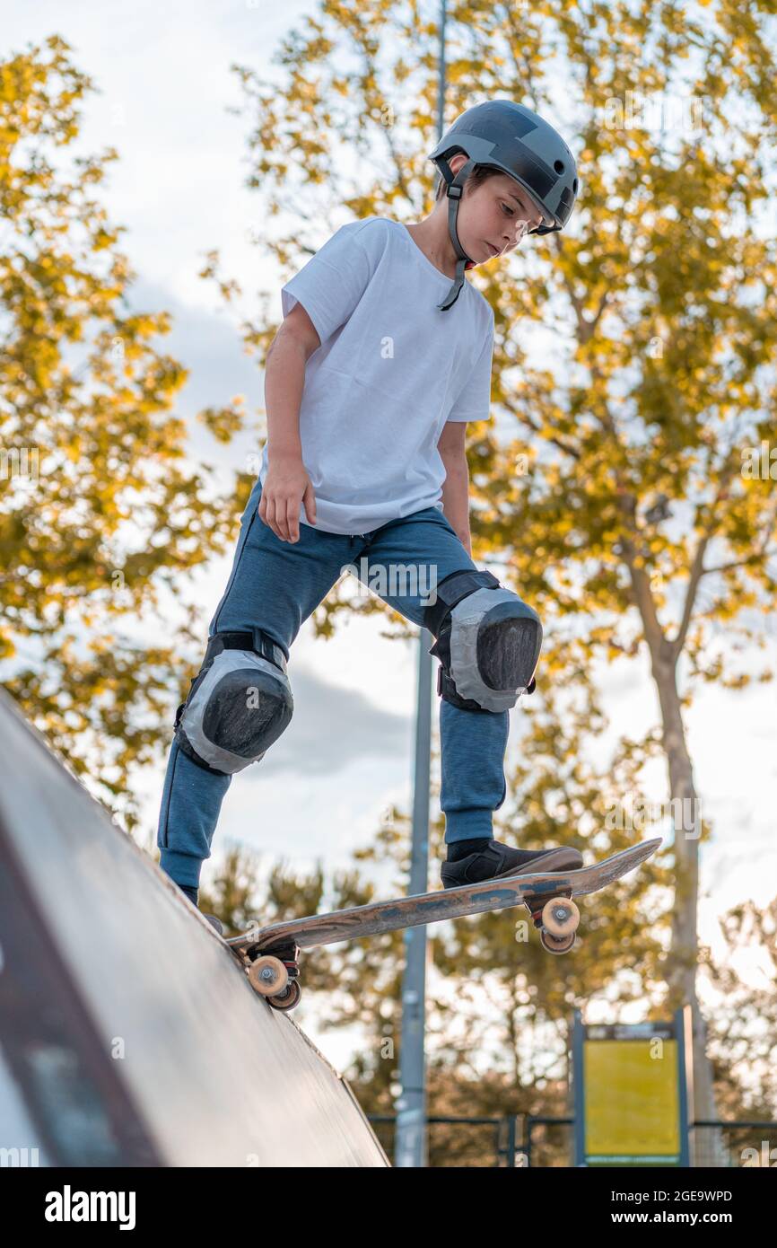 Low angle side view of brave teen skater standing on skateboard and ...