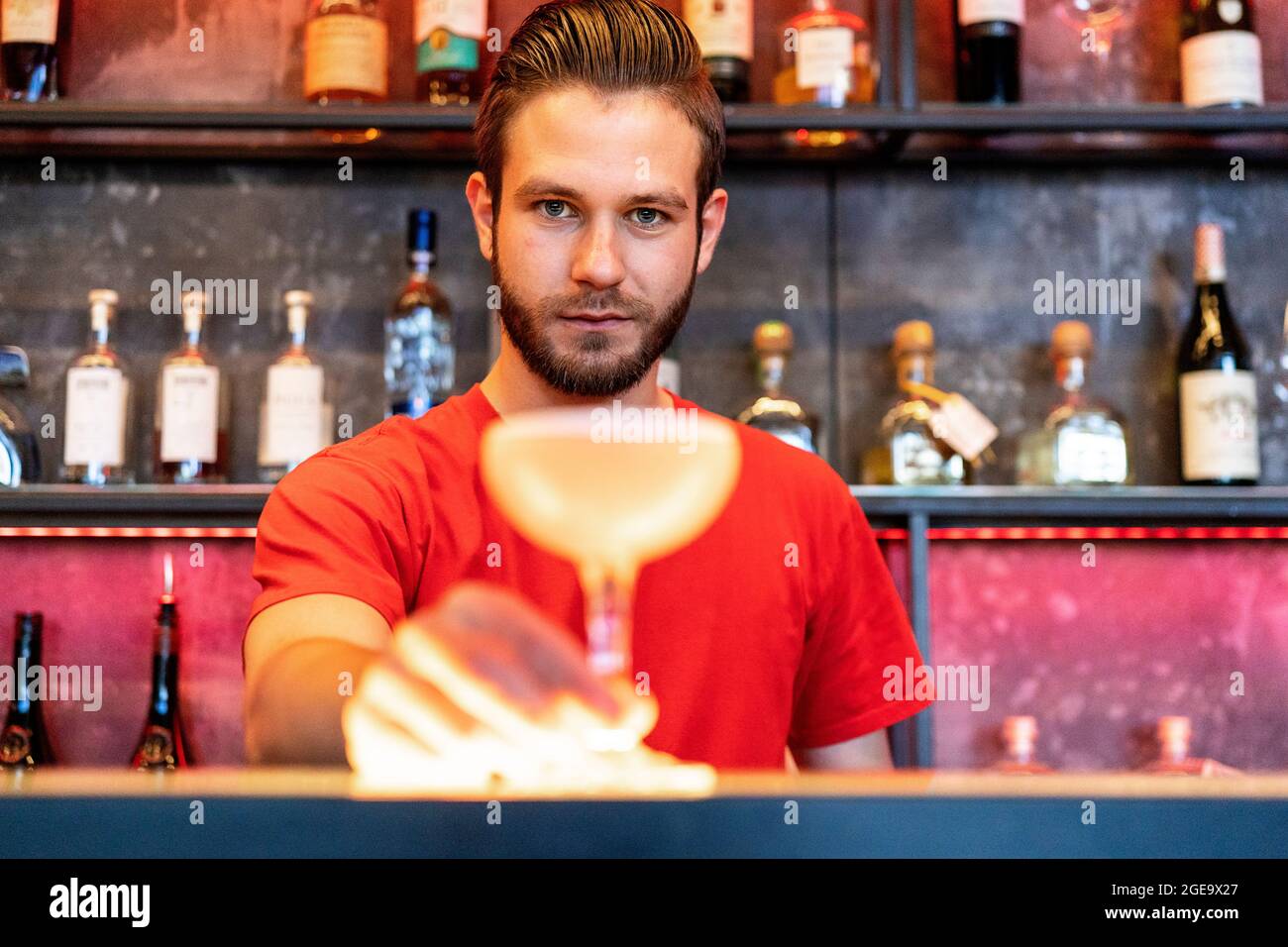 Cheerful barman serving glass with alcohol cocktail on counter in bar ...