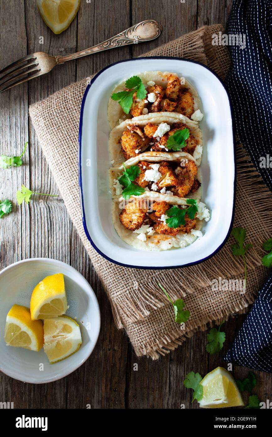 From above cauliflower snack tacos in bowl and lemon pieces in plate on ...