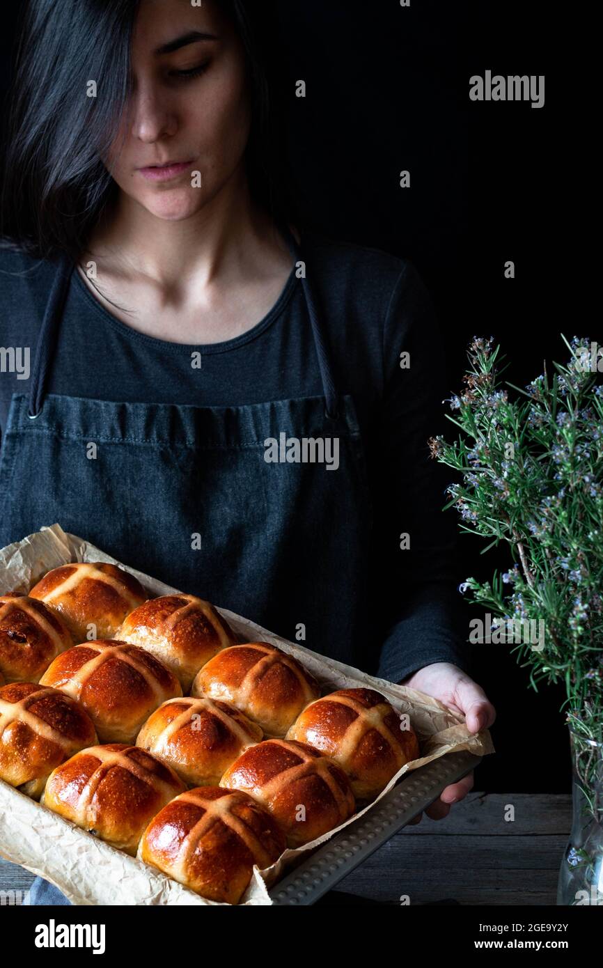 Female baker holding puff freshly baked hot cross buns on baking tray ...