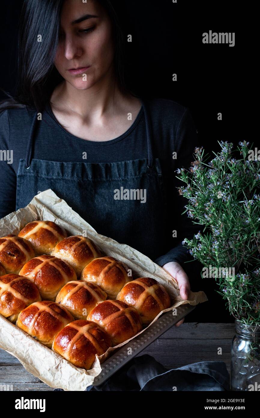 Female baker holding puff freshly baked hot cross buns on baking tray ...