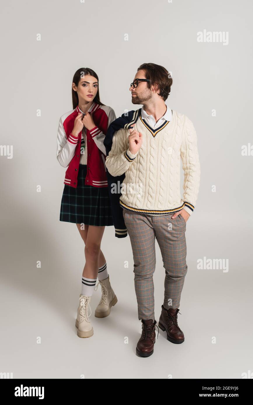 woman looking at camera near man in white knitted pullover on grey ...