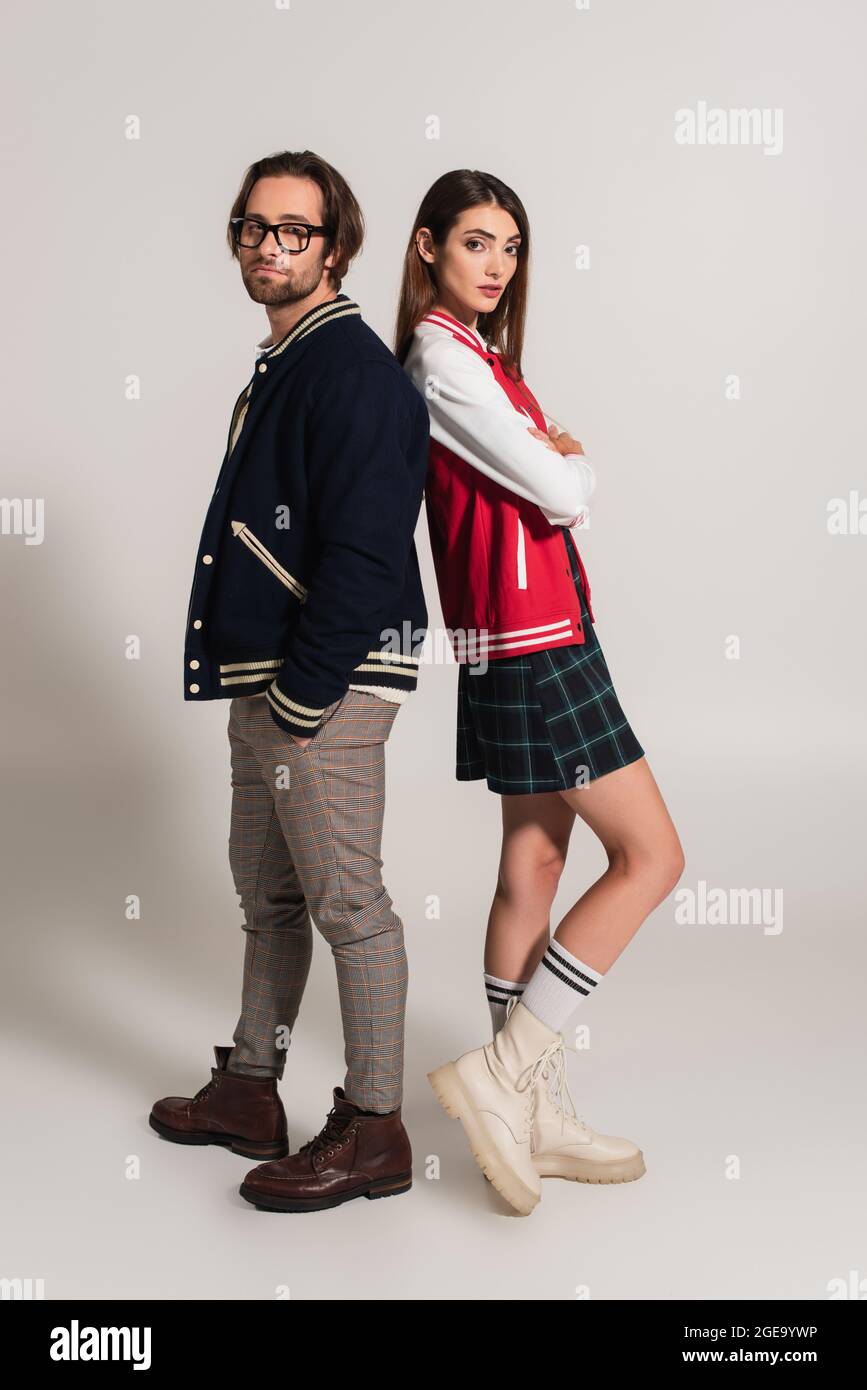 full length view of young couple in trendy clothes posing back to back ...