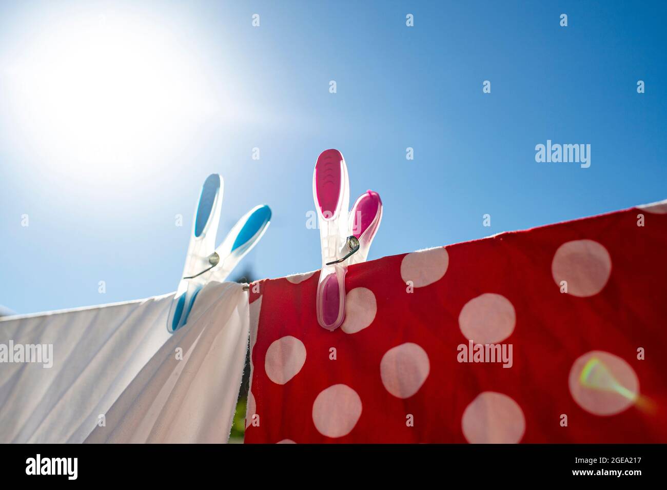 Two brightly coloured pegs holding washing on a line in bright sunshine ...