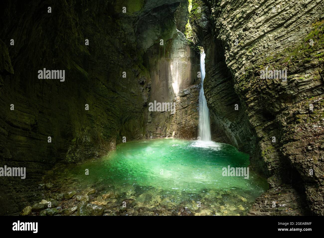 Crystal clear waterfall in a limestone cave flooded with sunlight and ...