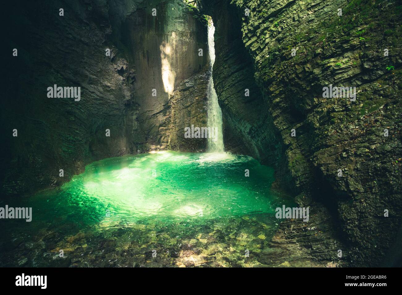 Crystal clear waterfall in a limestone cave flooded with sunlight and ...