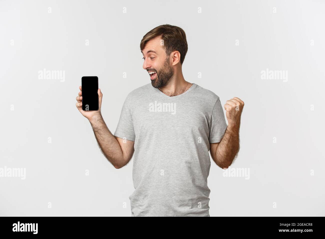 Portrait of excited man with beard, achieve goal in app, showing mobile ...