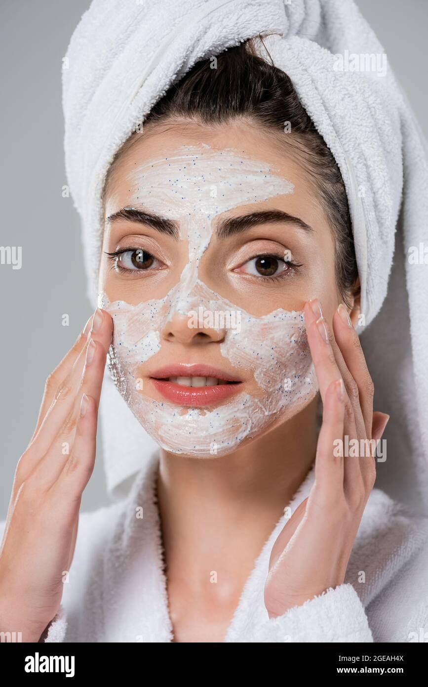 young woman with towel on head applying face scrub isolated on grey ...