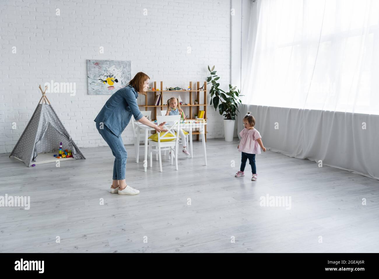 kindergarten teacher with outstretched hands standing near kid with ...
