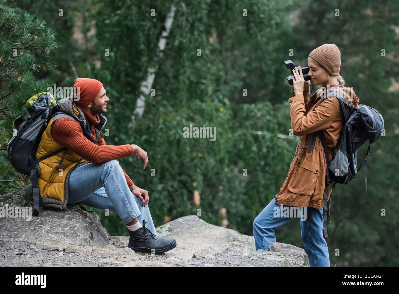 woman with backpack taking photo of happy boyfriend on vintage camera ...