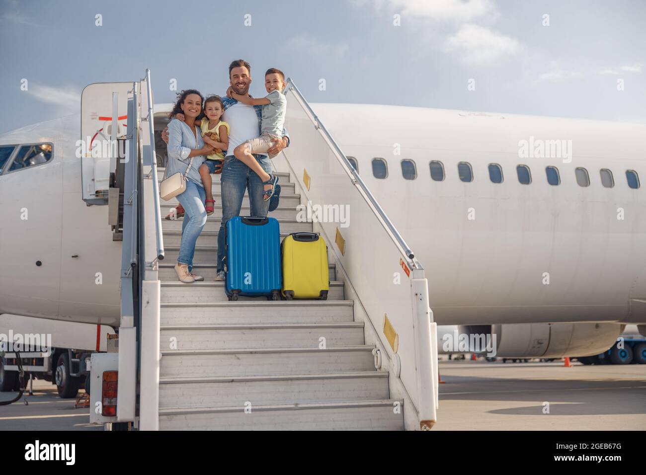 Happy family of four standing on airstairs, getting off the plane on a ...