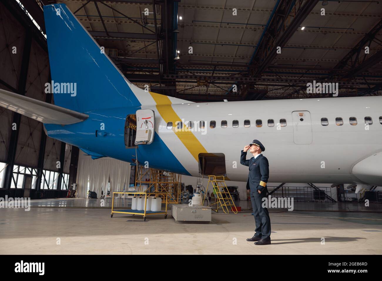 Proud pilot in uniform looking away, adjusting his hat, standing in ...