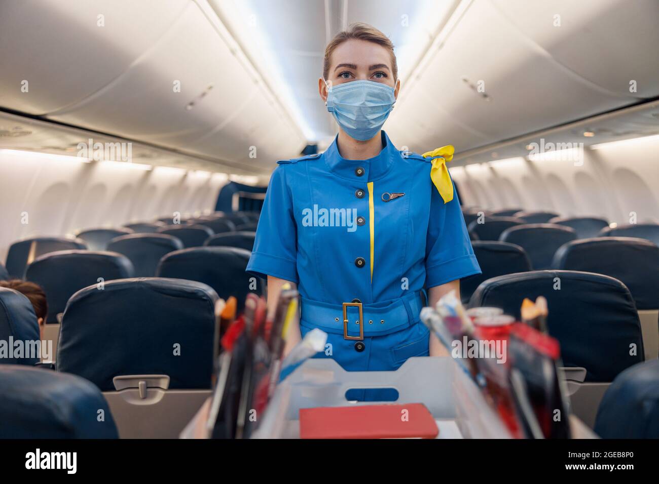 Stewardess in protective face mask and blue uniform serving food to ...