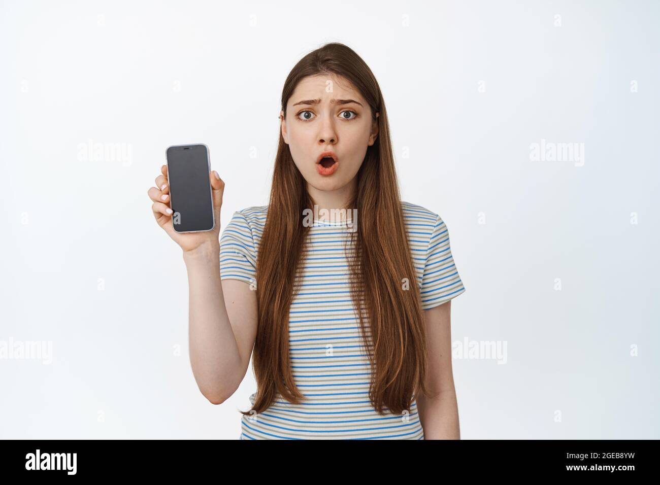 Shocked caucasian girl shows smartphone screen with worried face ...