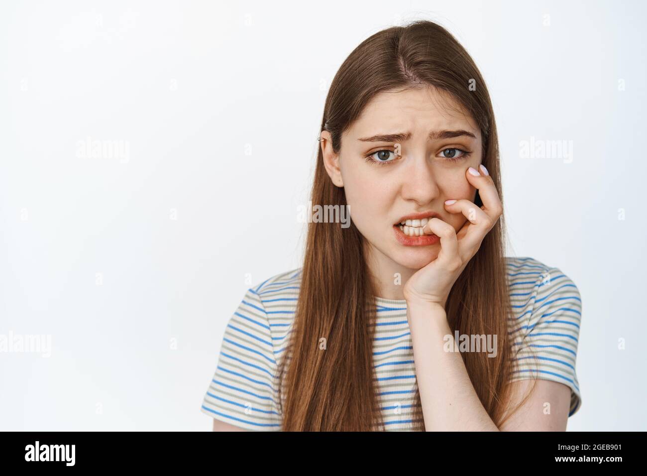Portrait of scared girl biting her finger, looking anxious and worried ...