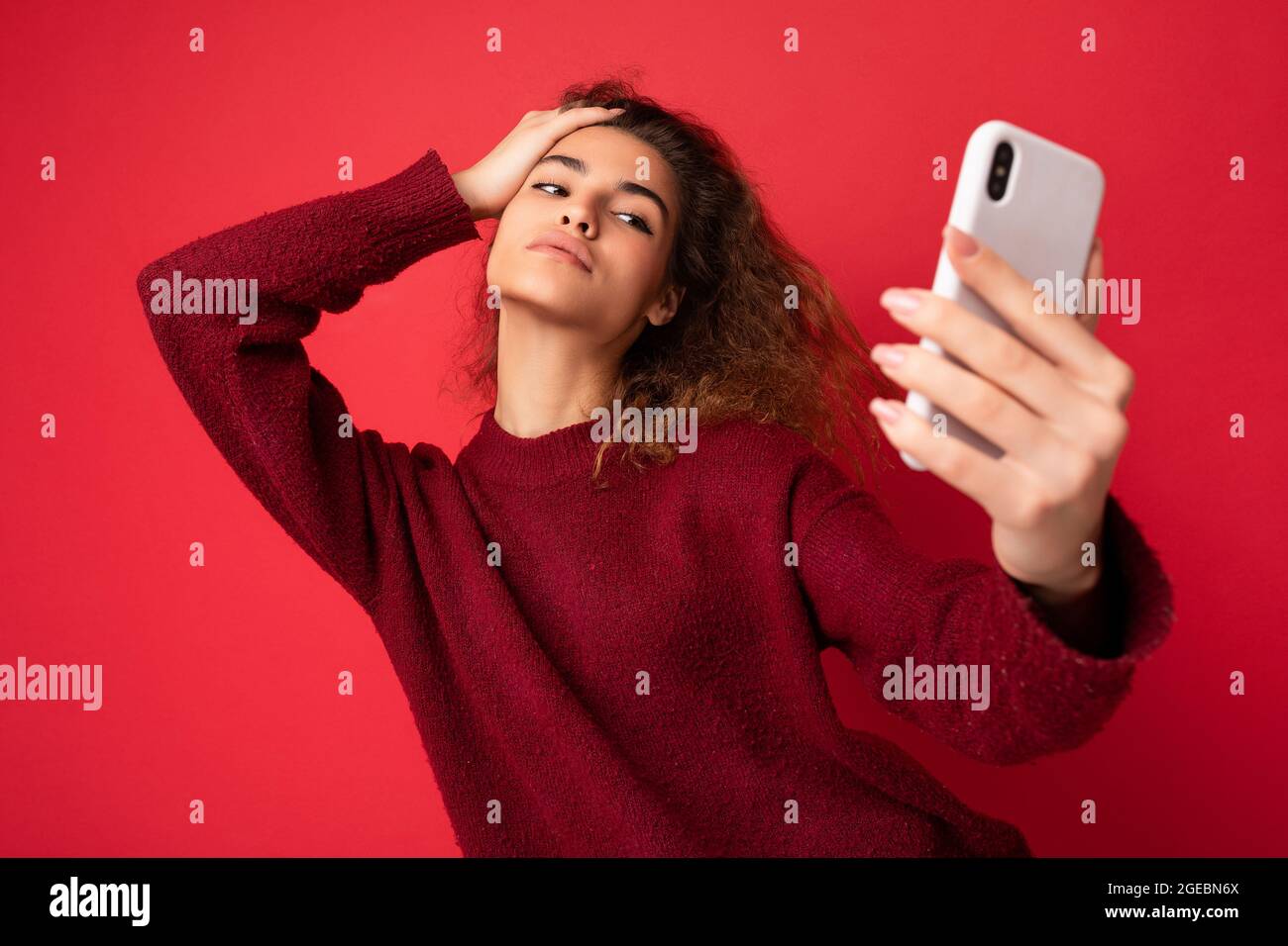 Beautiful young woman with curly hair wearing dark red sweater isolated ...