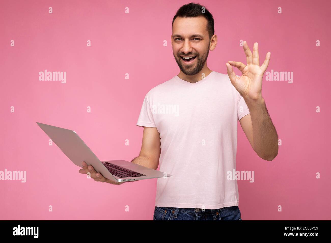 Handsome happy and funny brunet man holding laptop computer and showing gesture okay looking at ...