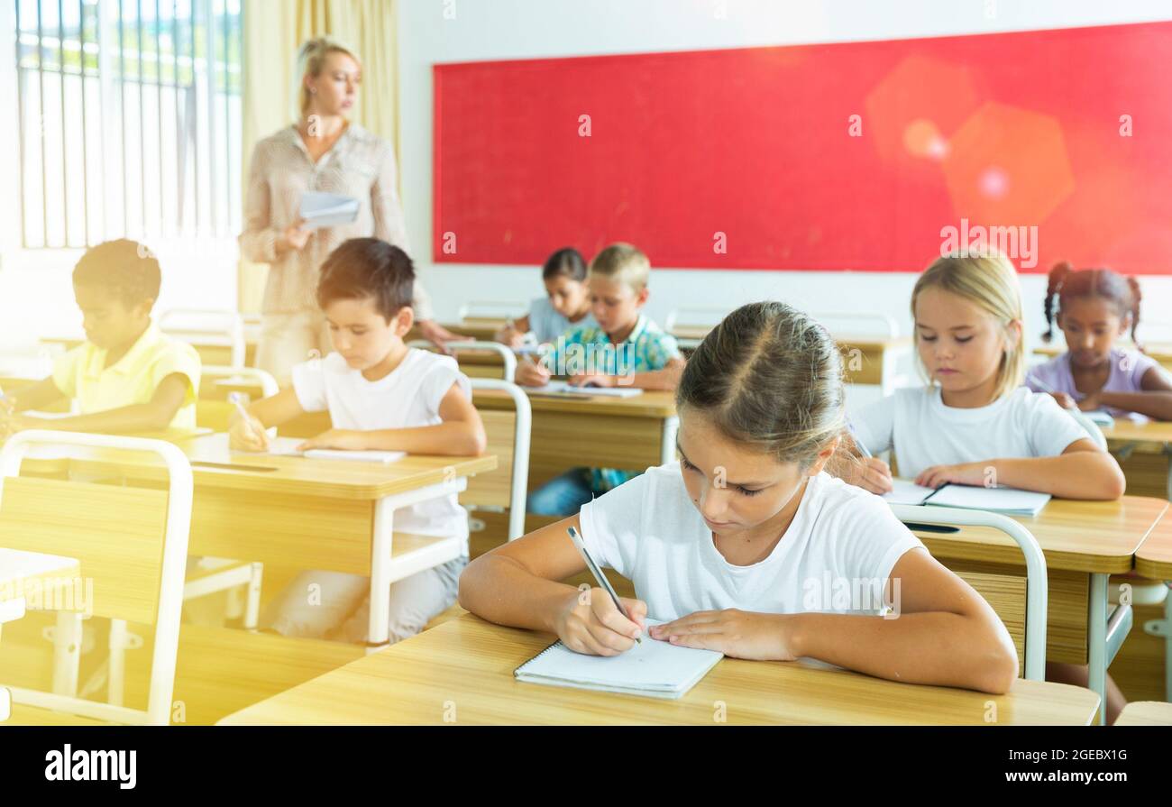 Preteen girl listening to teacher and writing in notebook in class ...