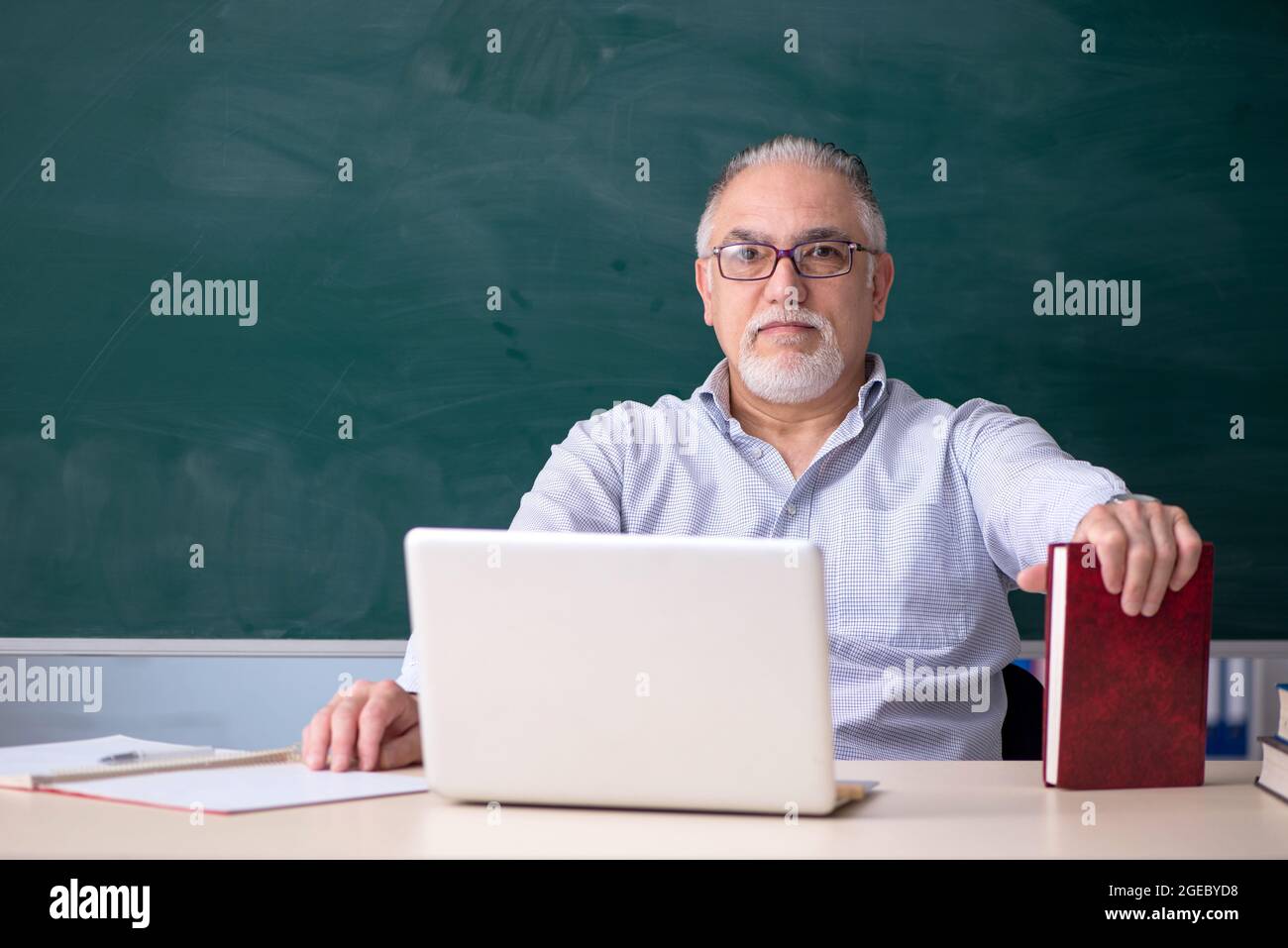 Old teacher in front of green board Stock Photo - Alamy