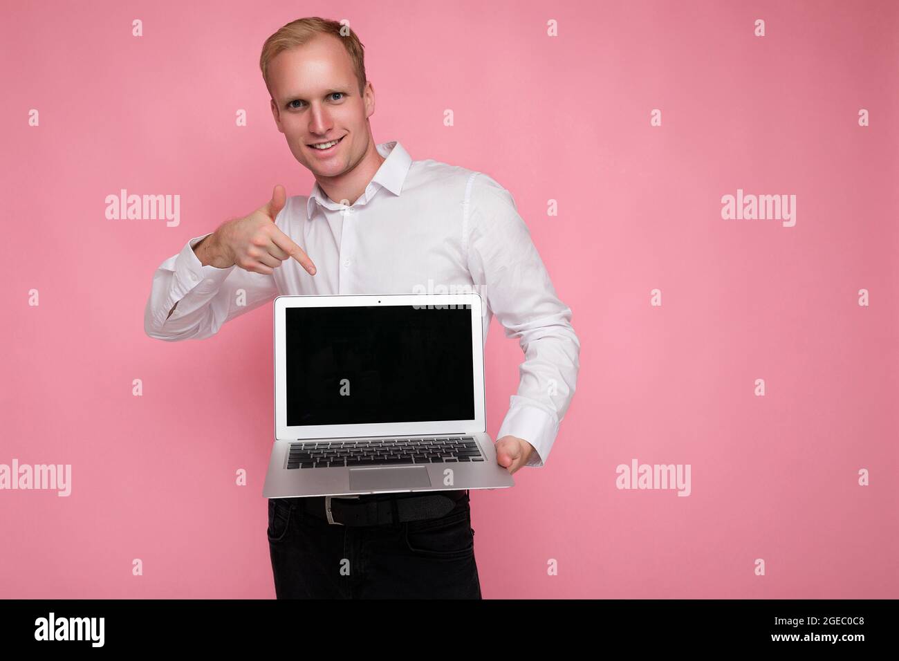 Photo shot of handsome smiling blonde man holding computer laptop with ...