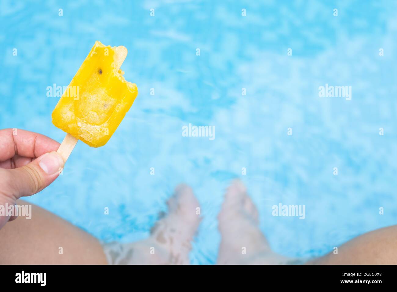 man sitting on the edge of an outdoor swimming pool and eating a ...