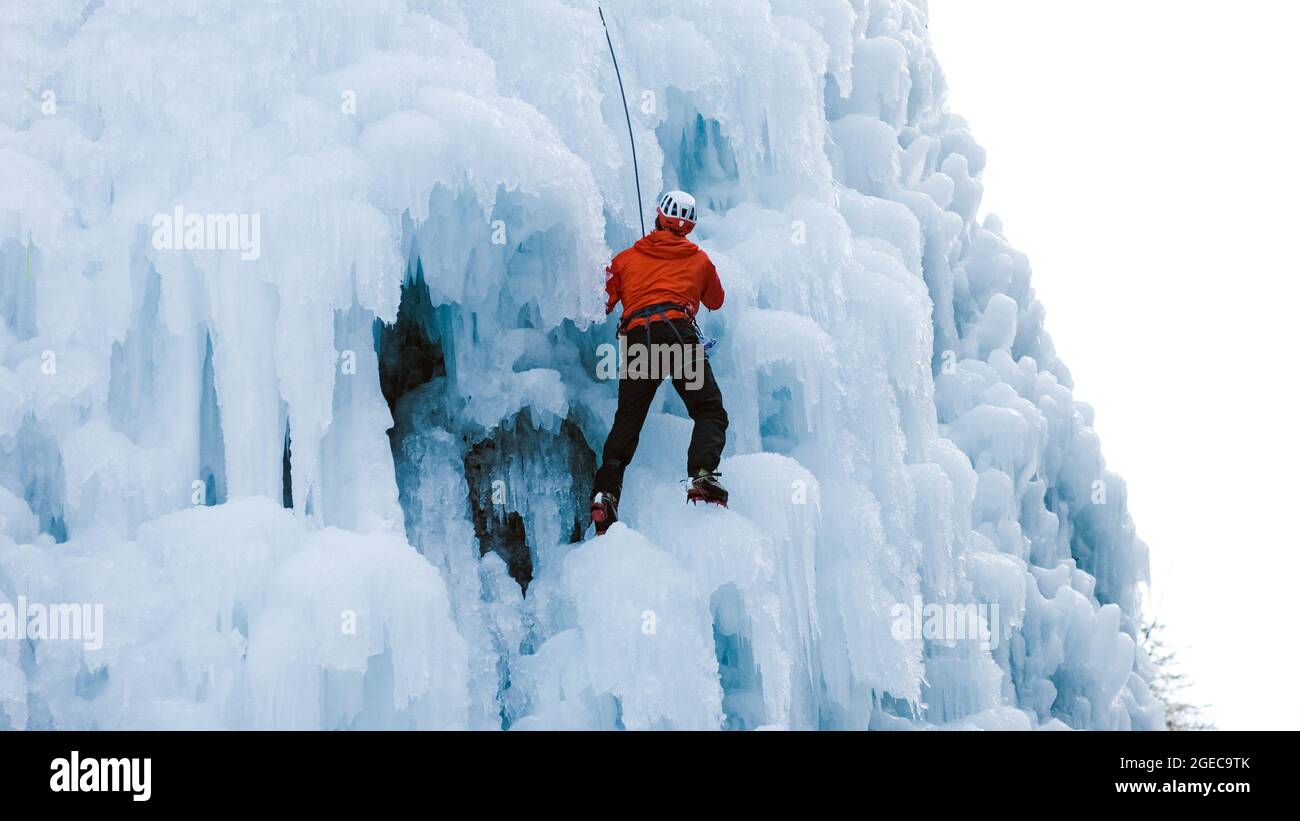 Aerial shot of a frozen ice waterfall, and the male climber progresses ...