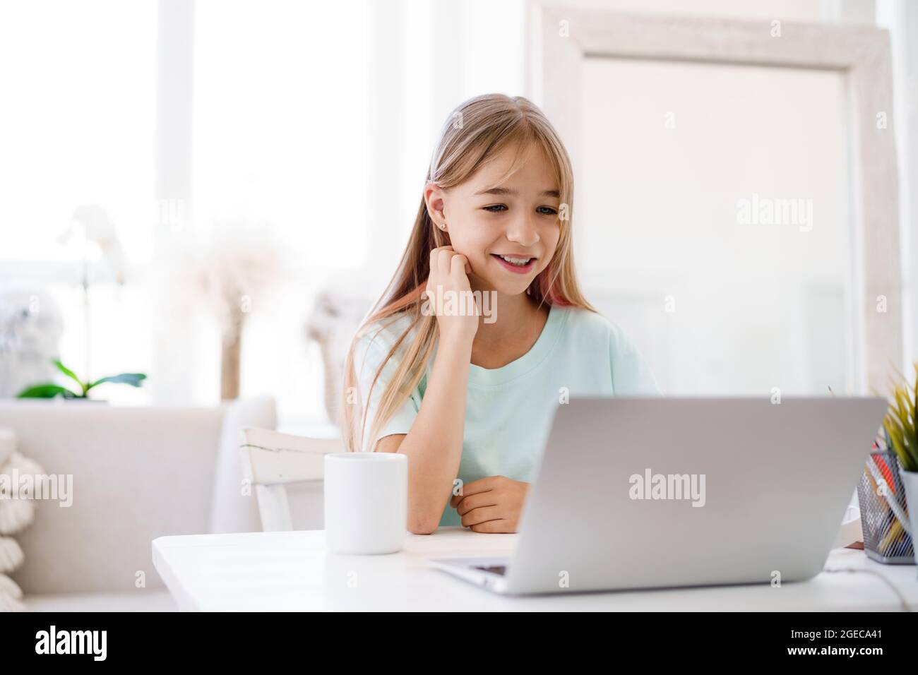 Happy little girl pupil using laptop at home Stock Photo - Alamy