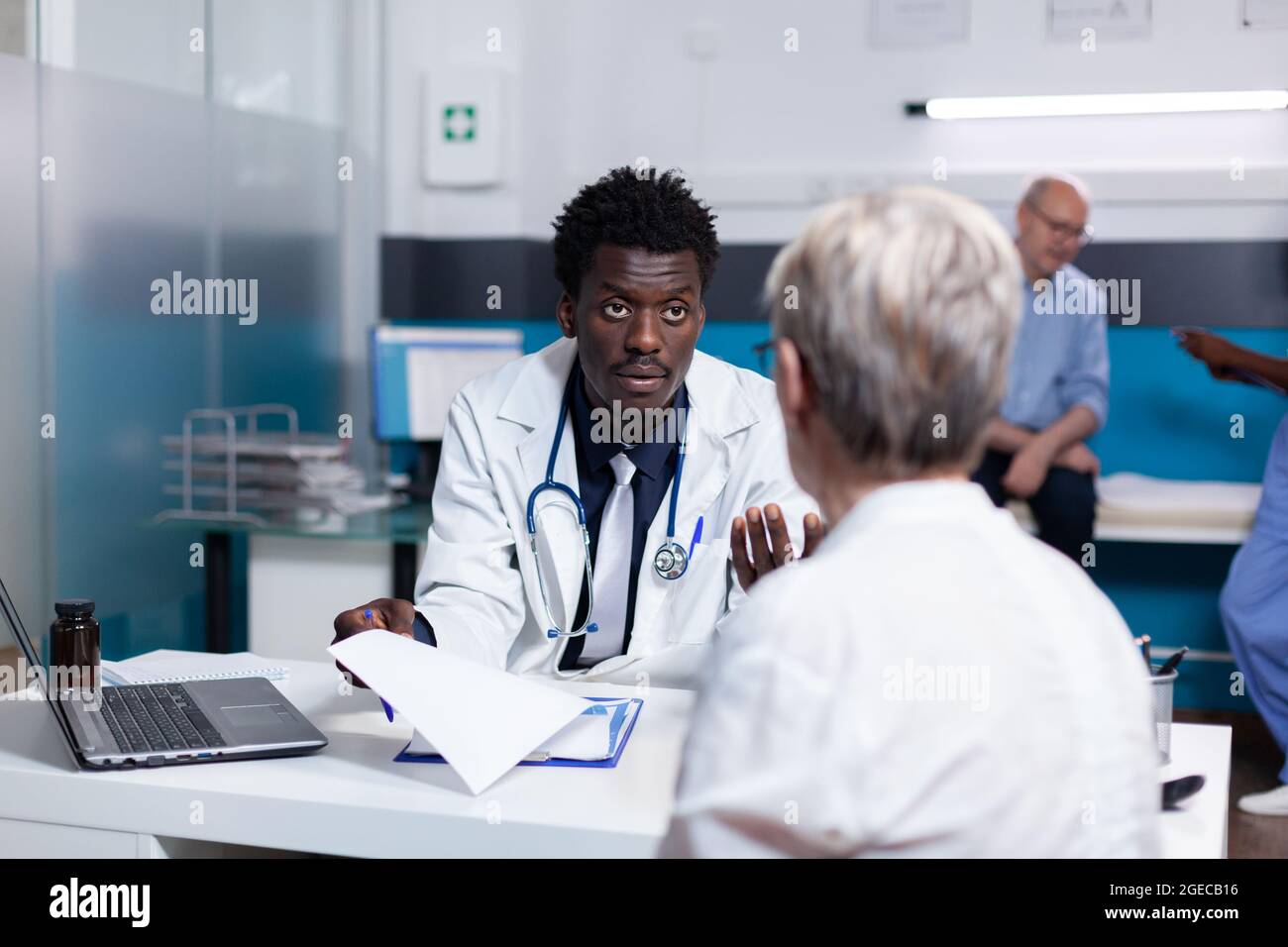 Black medical specialist consulting elderly patient at desk in doctors ...