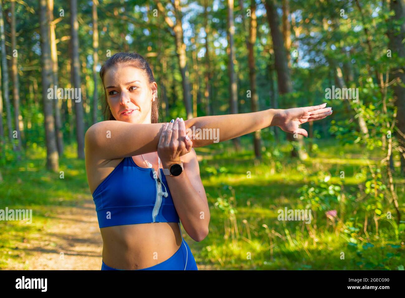 Woman runner stretching arms before exercising in a summer park morning ...