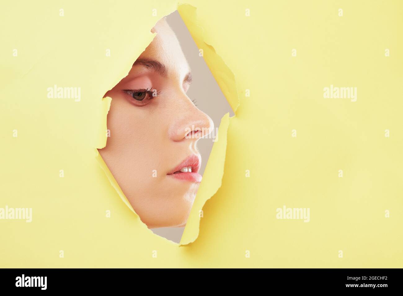 Side view of serious young female face appearing in hole of ripped ...