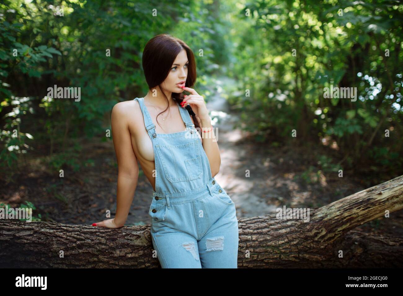 Young woman in jeans overalls standing under tree in woodland Stock ...