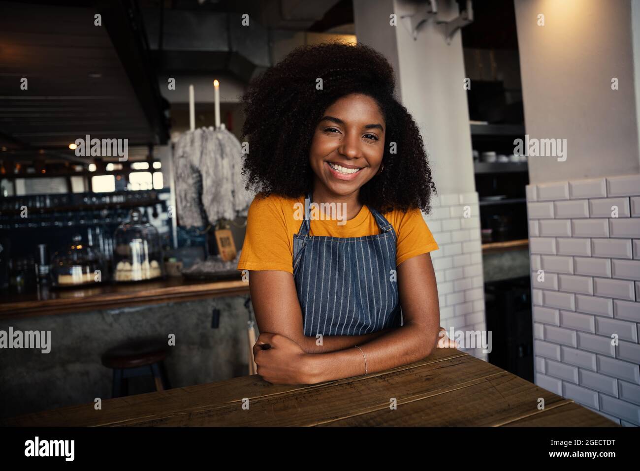 Beautiful mixed race female waitress wearing apron sitting at coffee ...