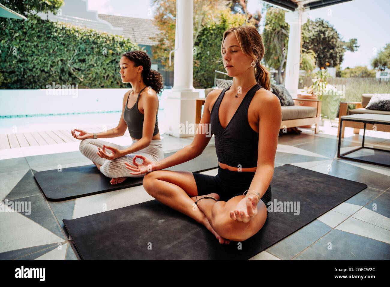 Two friends practicing meditation sitting cross legged outside home ...