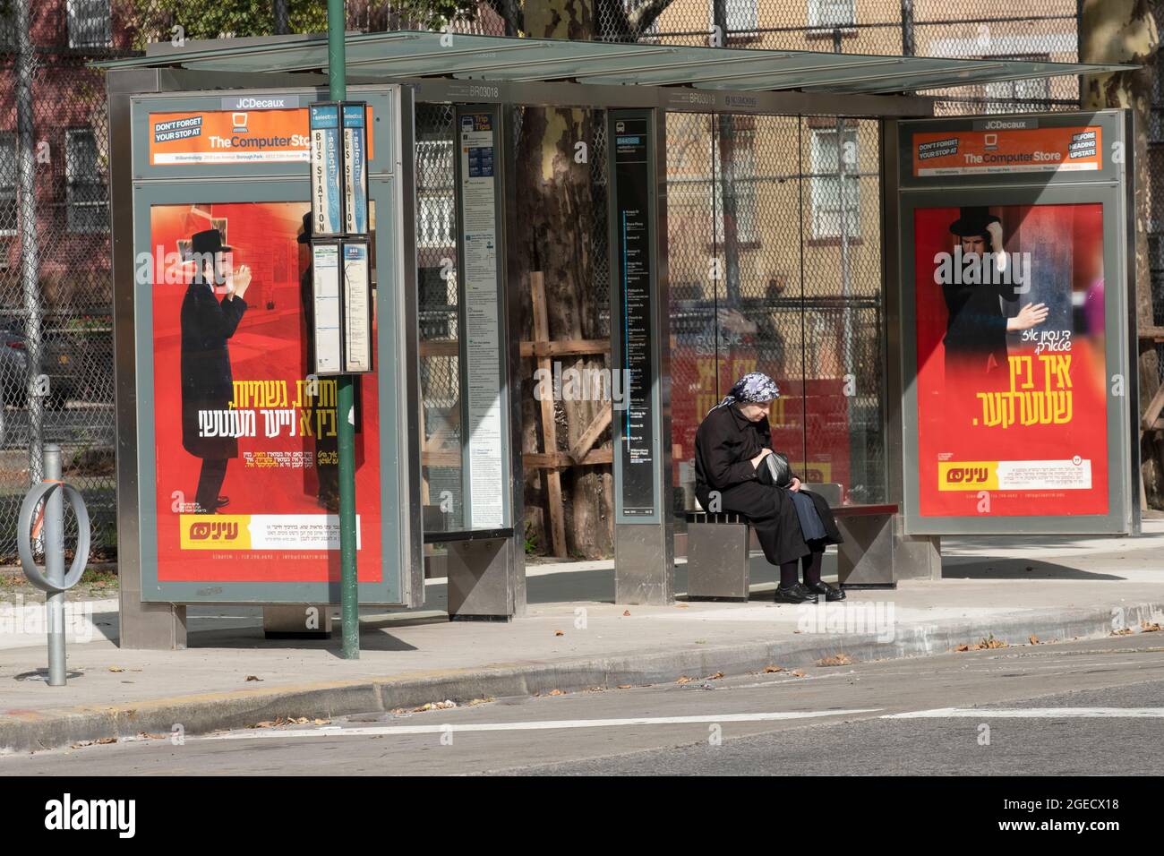 An ulltra orthodox Jewish woman waits on a bus stop bench surrounded by ...