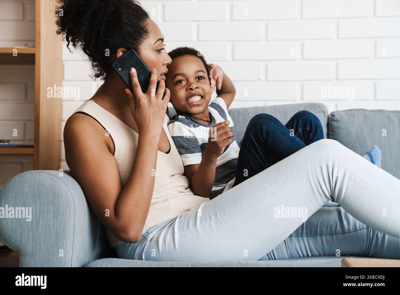 Black woman talking on cellphone while hugging her son at home Stock ...