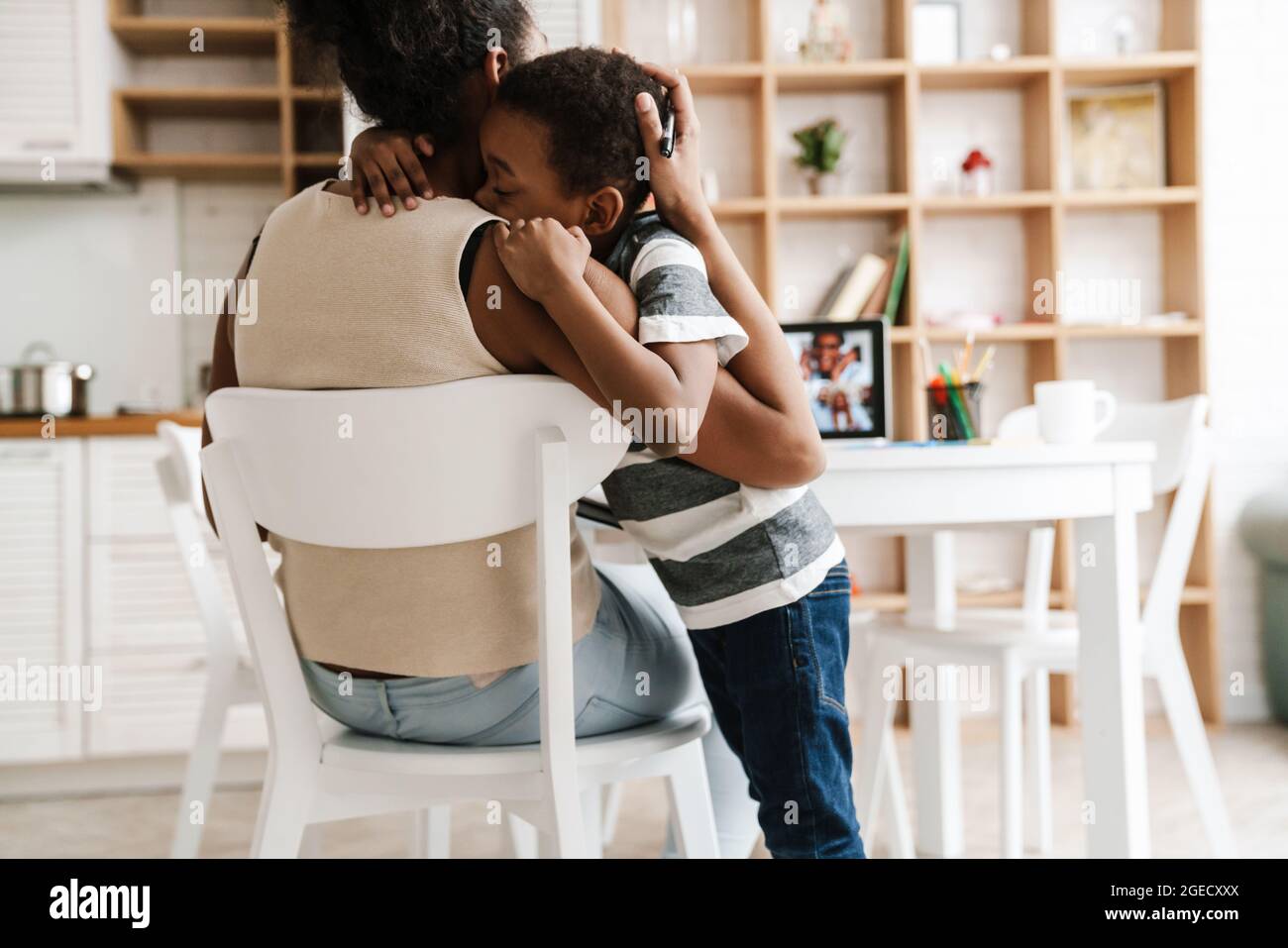 Black woman hugging her son while working with laptop at home Stock ...